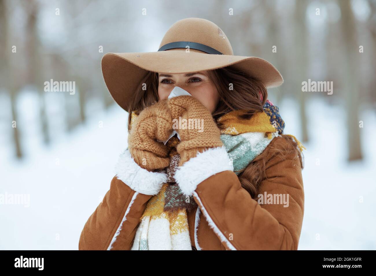 modern middle aged woman in brown hat and scarf with mittens and napkin ...