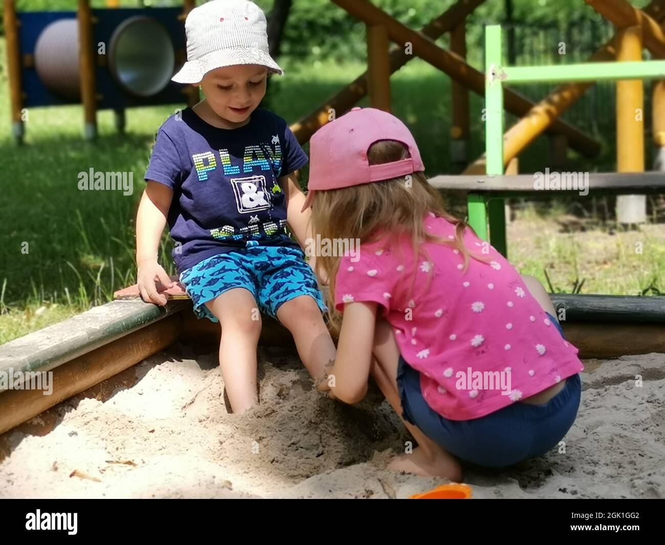 Two children playing on a sandy playground surrounded by green grass ...