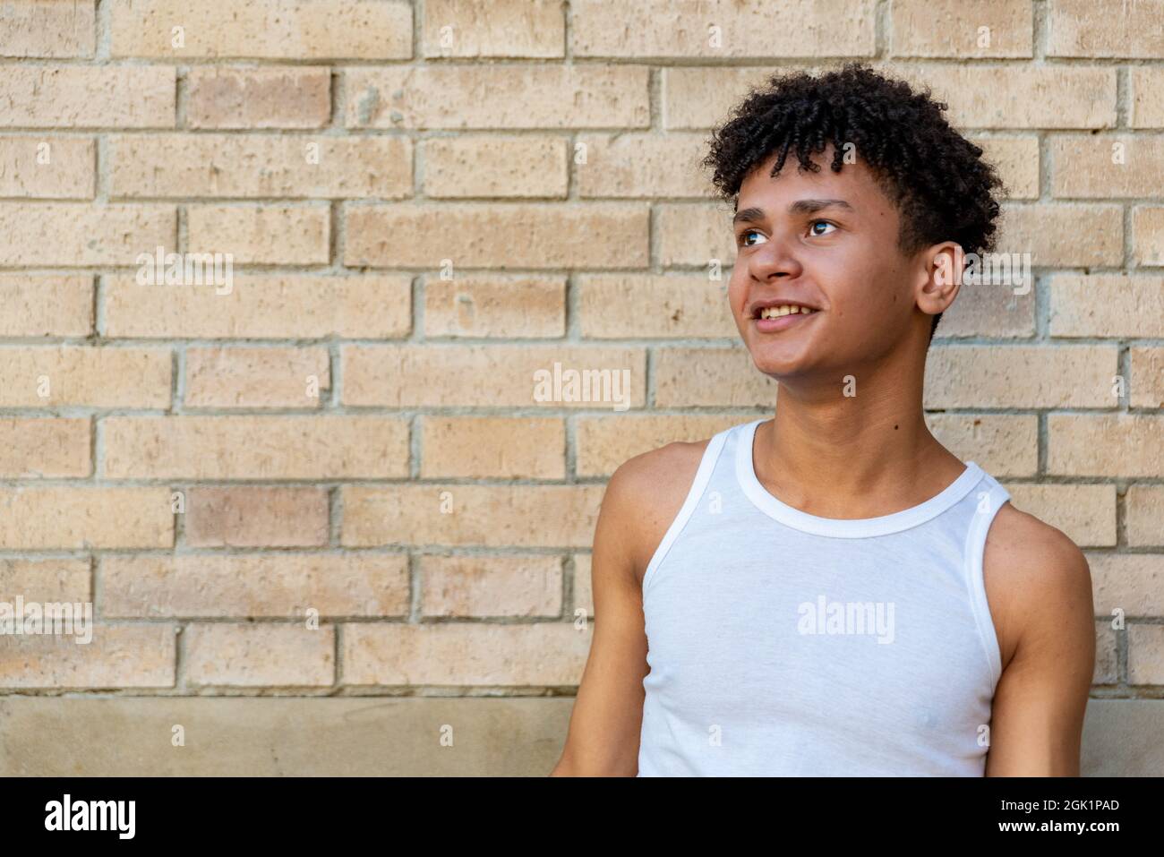 Afro latin male teenager smiling against a brick wall Stock Photo - Alamy