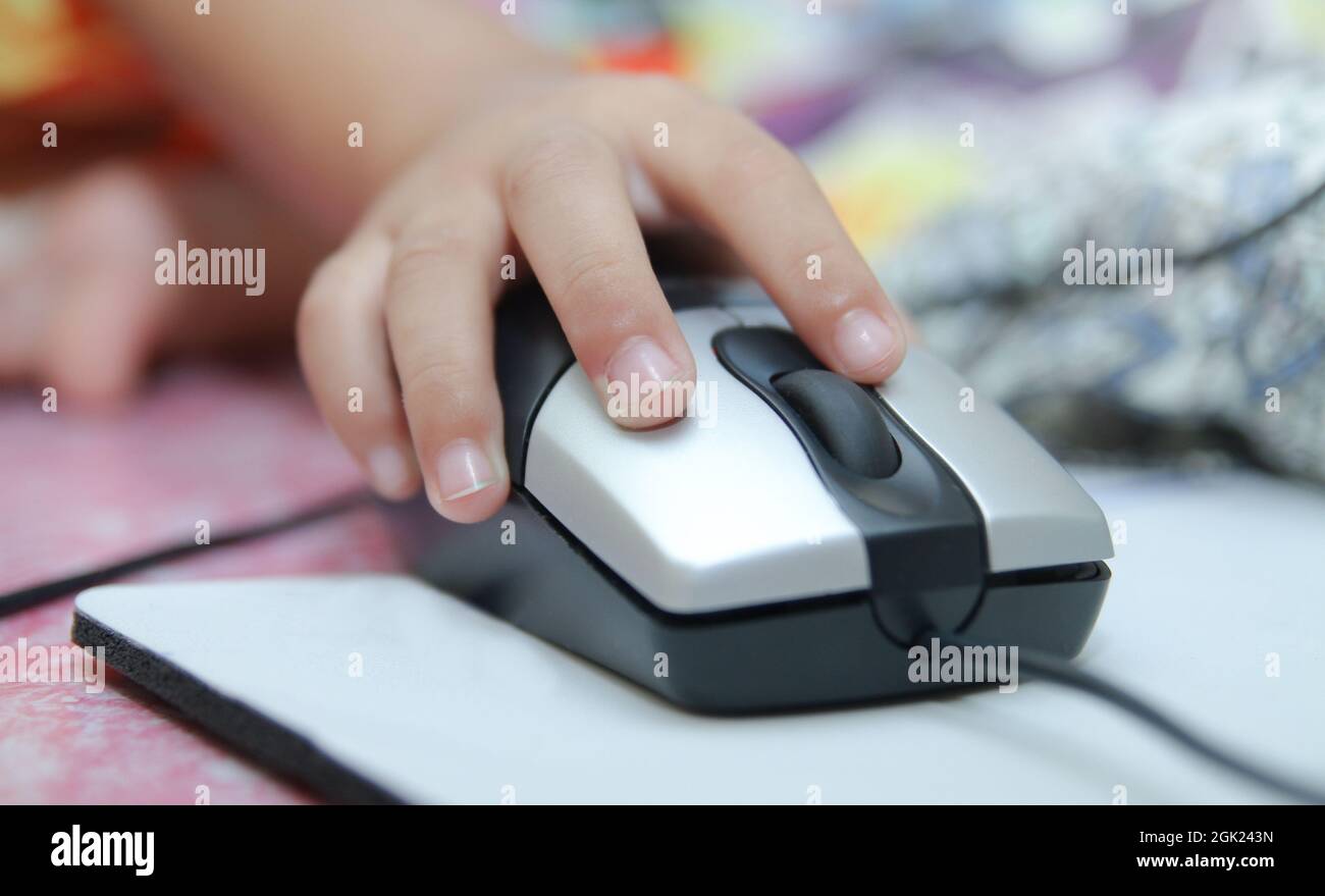 Child hand holds a computer mouse or keyboard. Child learns online and ...