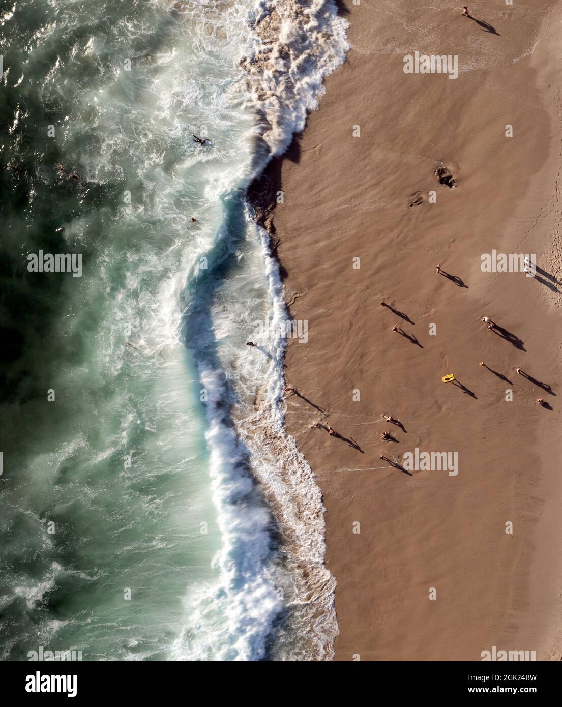 Top down view of people casting shadows on sandy beach with ocean waves ...