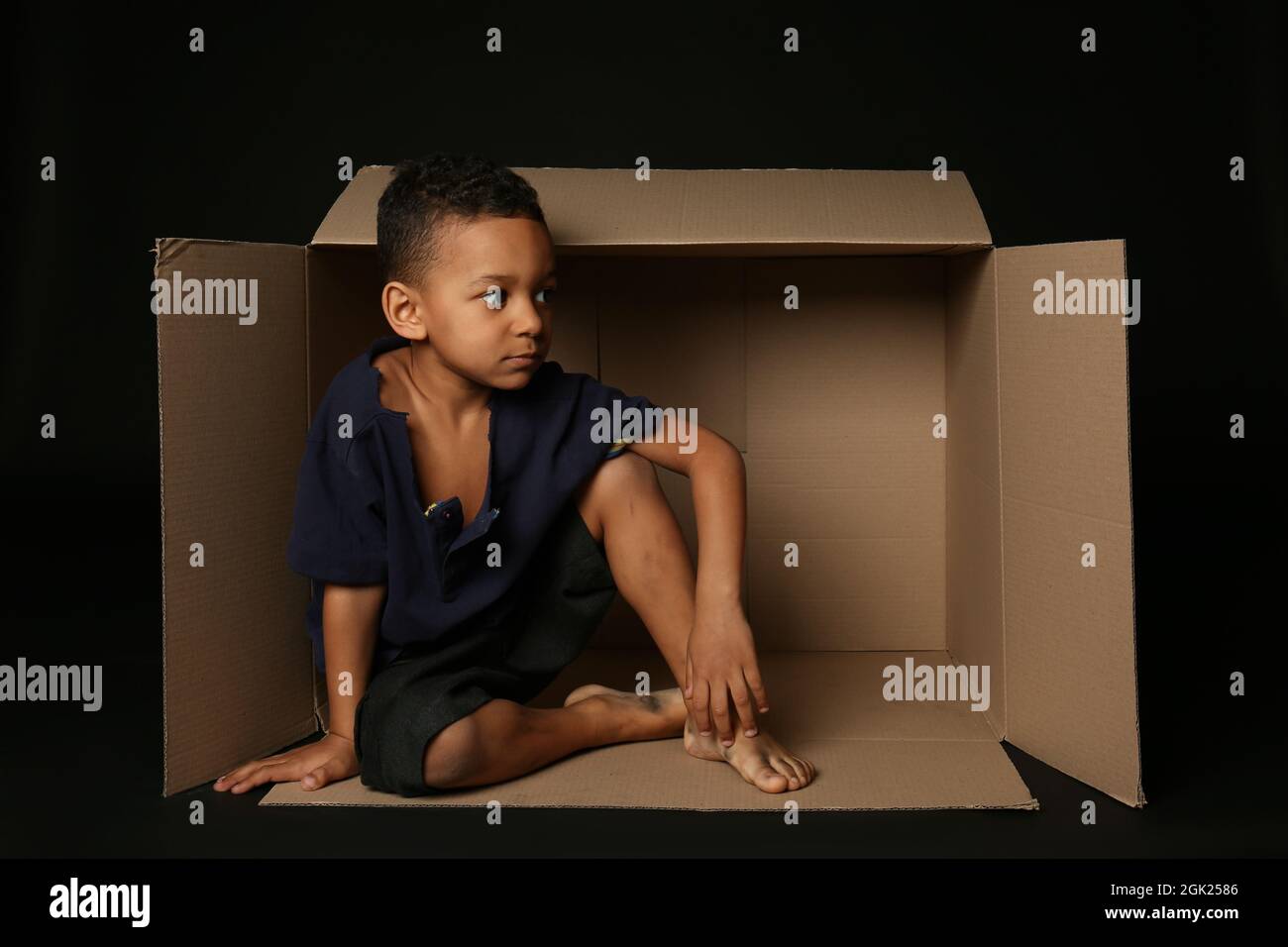 Cute little boy living in box on dark background. Poverty concept Stock ...