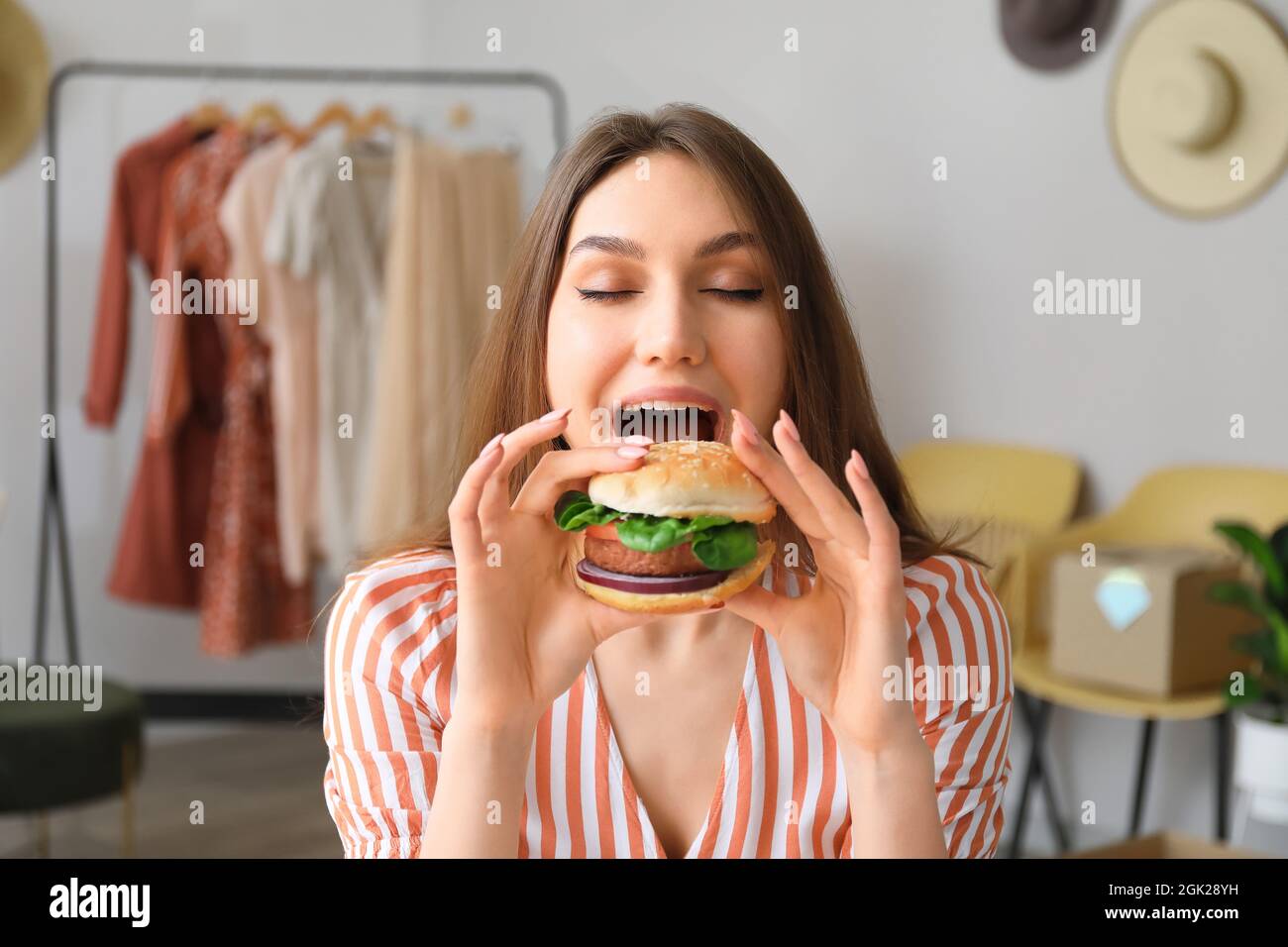 Female seller eating tasty vegan burger at workplace Stock Photo - Alamy
