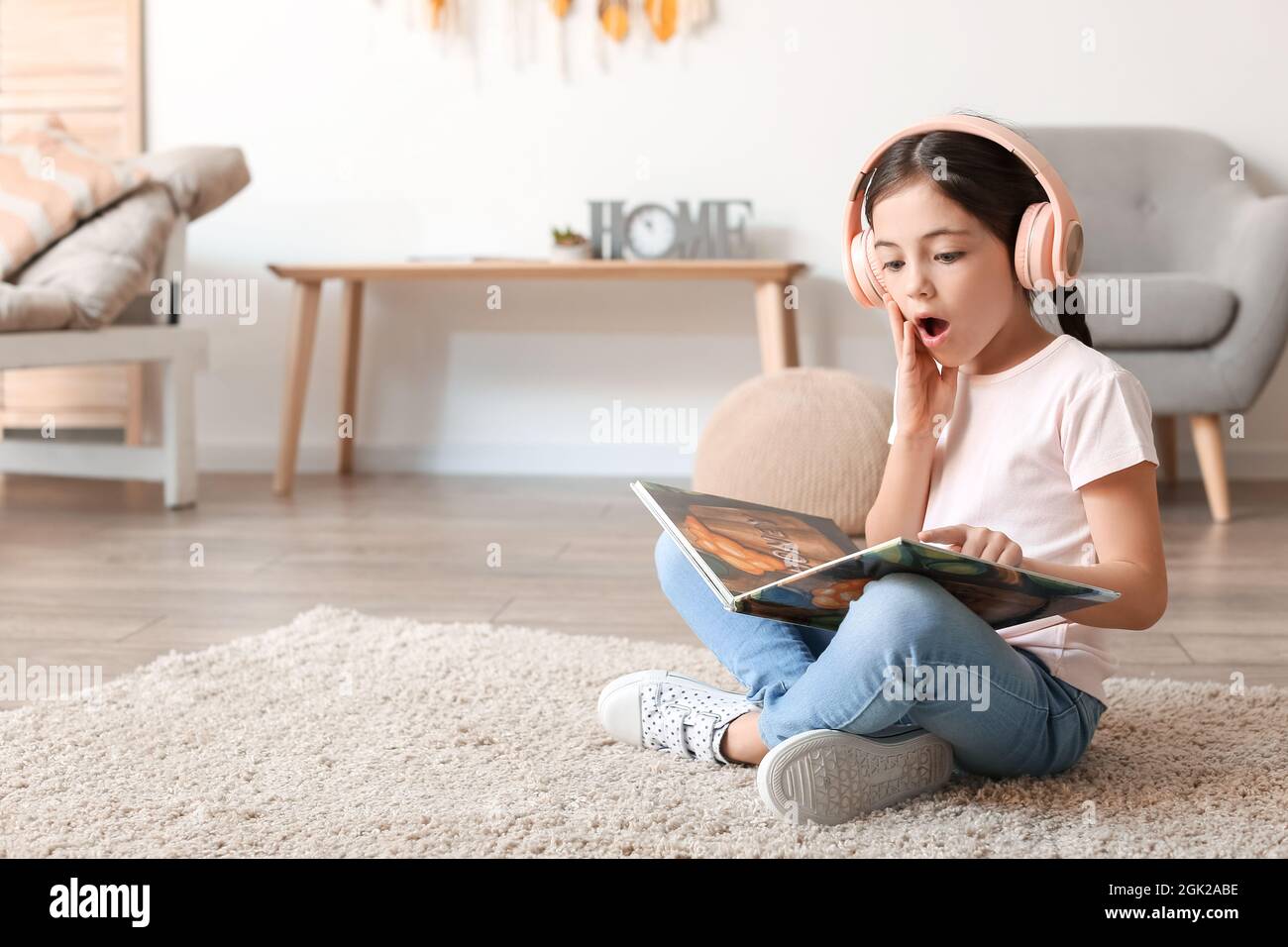 Surprised little girl with headphones reading book at home Stock Photo ...
