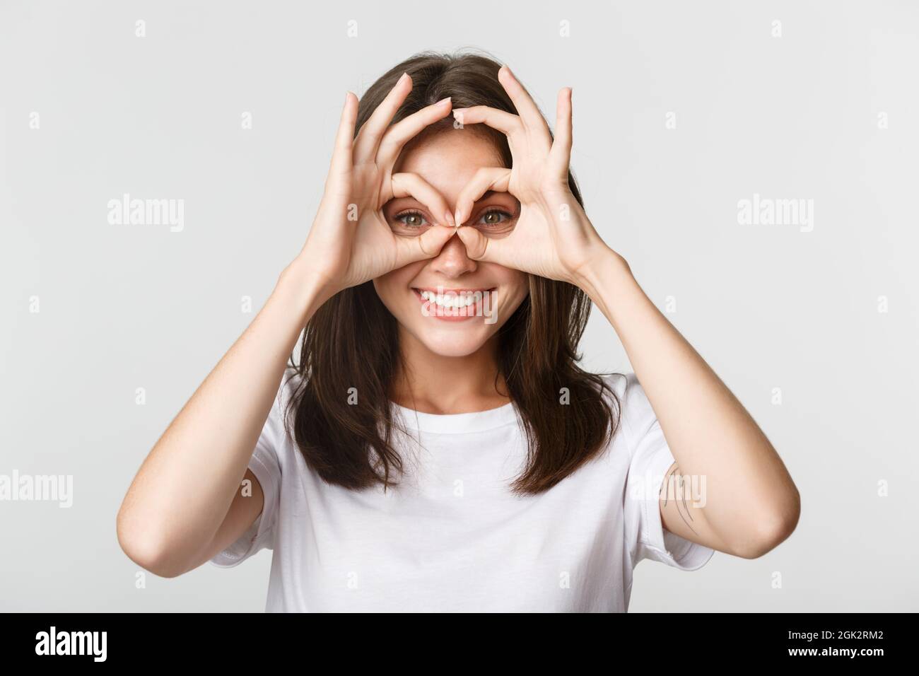 Close-up of happy smiling brunette girl looking through okay gestures ...