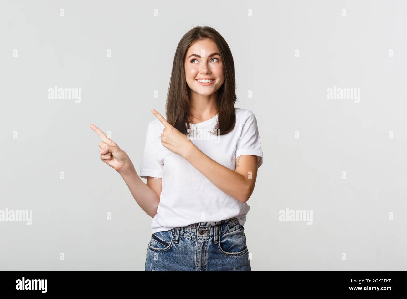 Dreamy beautiful girl smiling, pointing fingers upper left corner and ...