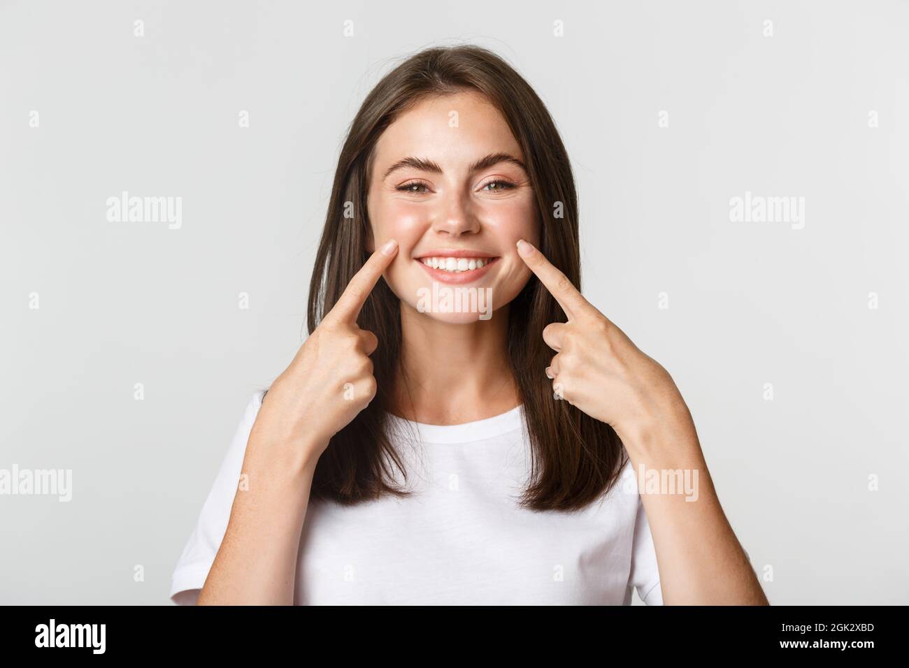 Close-up of attractive smiling young girl pointing fingers at face ...