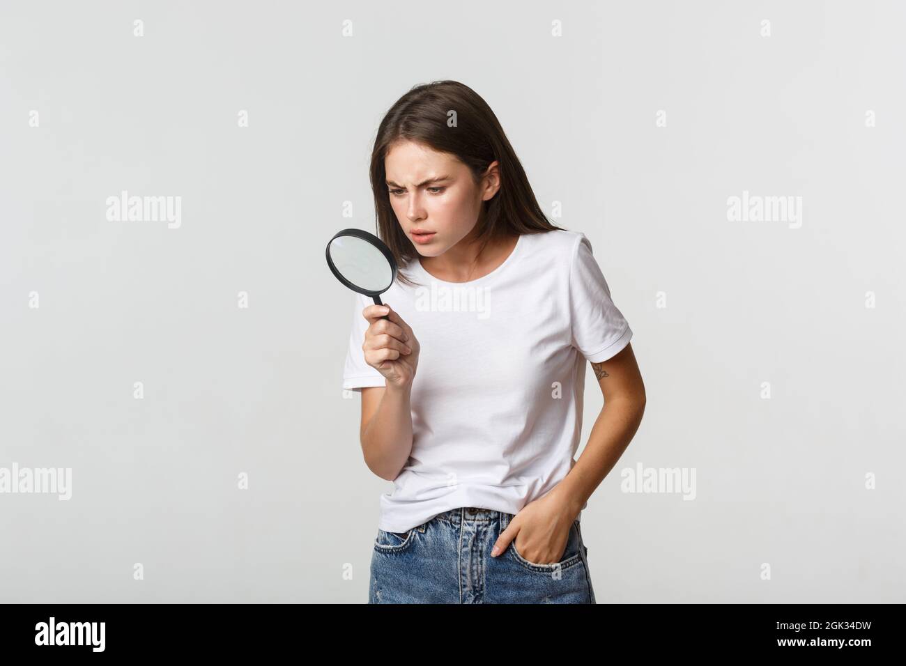 Serious-looking smart beautiful girl looking through magnifying glass ...
