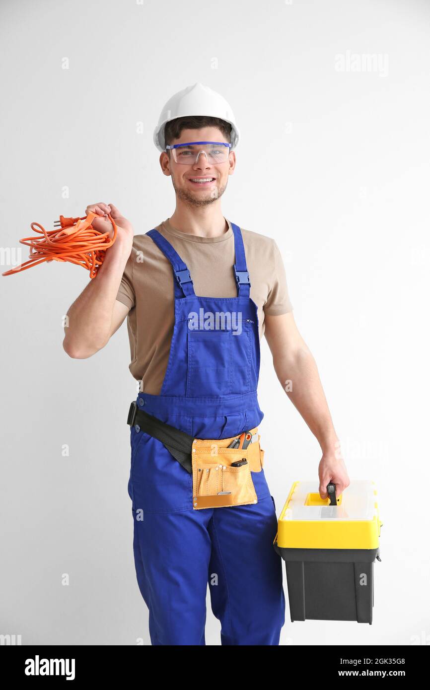 Young smiling electrician with bunch of wires and toolbox on white ...