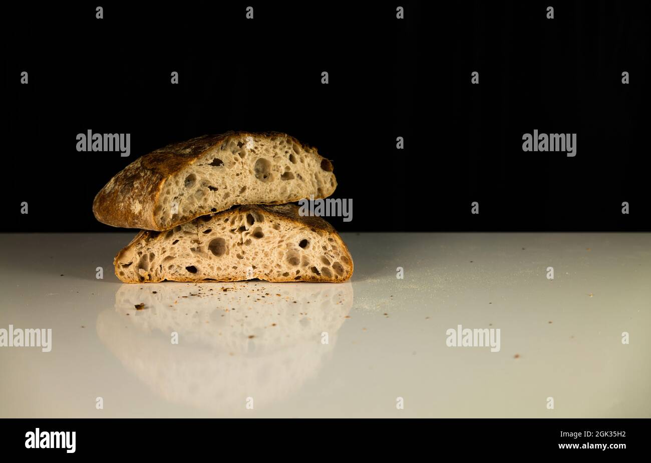 Bread cut in half on white table against black background Stock Photo ...