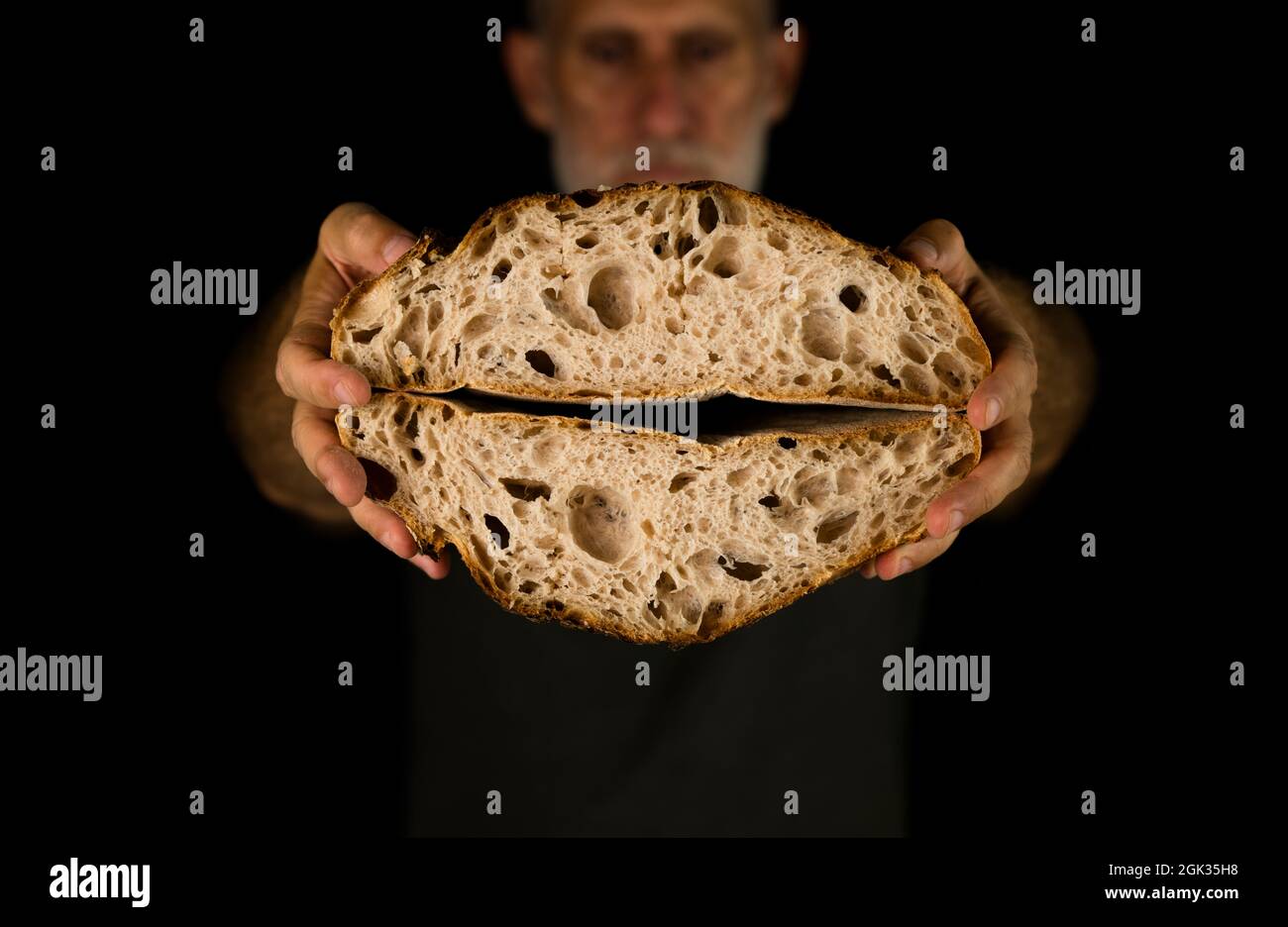 Adult man holding bread cut in half against black background Stock ...