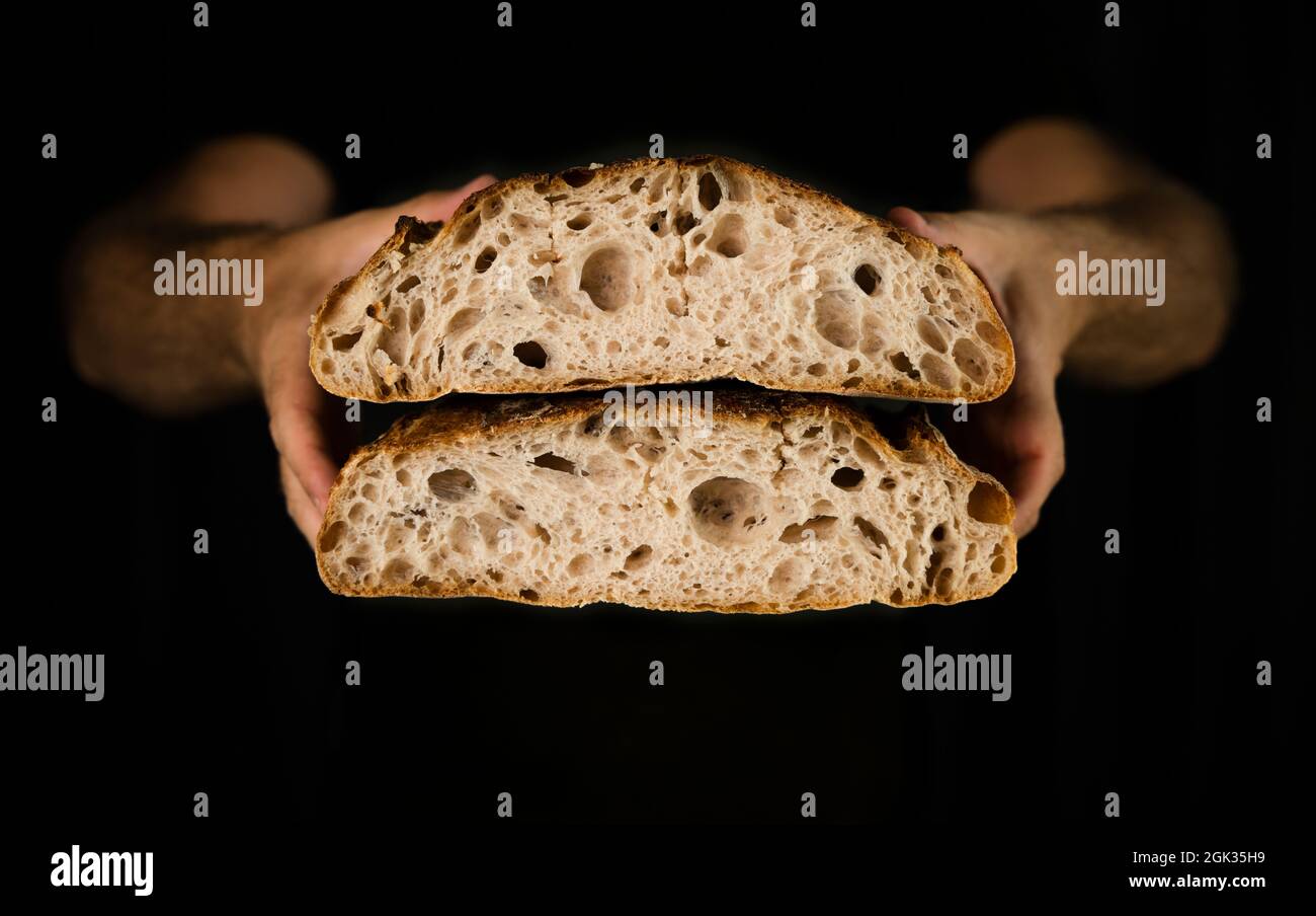Adult man holding bread cut in half against black background Stock ...