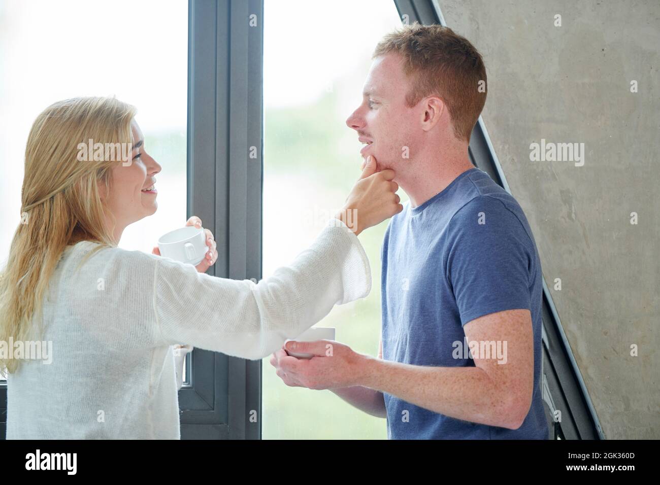 Smiling young woman with cup of coffee in hand wiping crumb off chin of ...