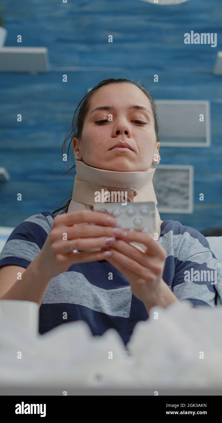 Close up of person with cervical neck collar looking at capsule tablets ...