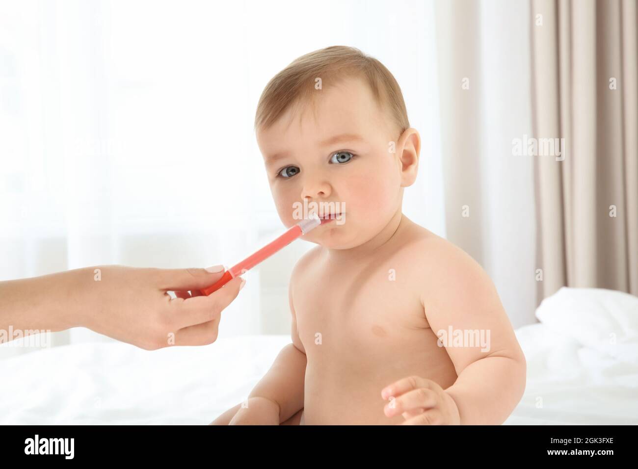 Mother holding oral dosing syringe and cute little baby sitting on bed ...