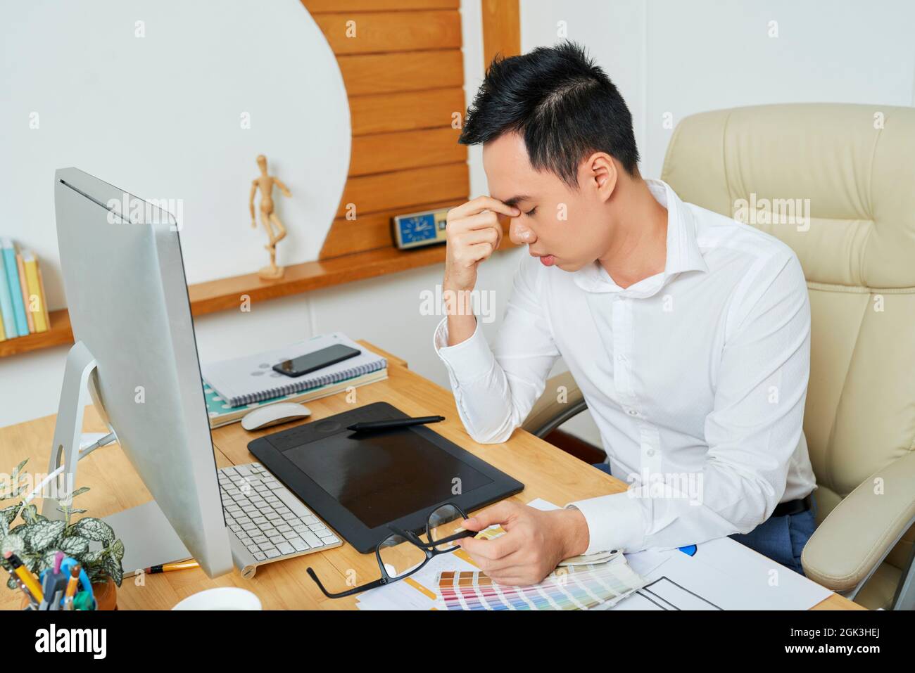 Tired young Vietnamese graphic designer having headache after working ...