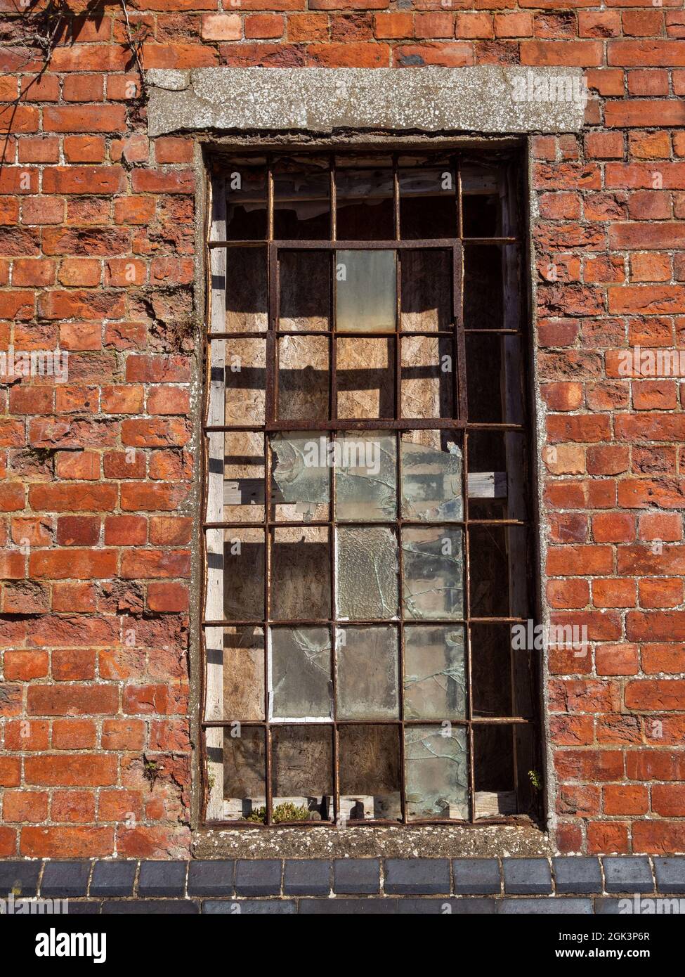Metal framed window with broken glass, partly boarded up, in a derelict ...