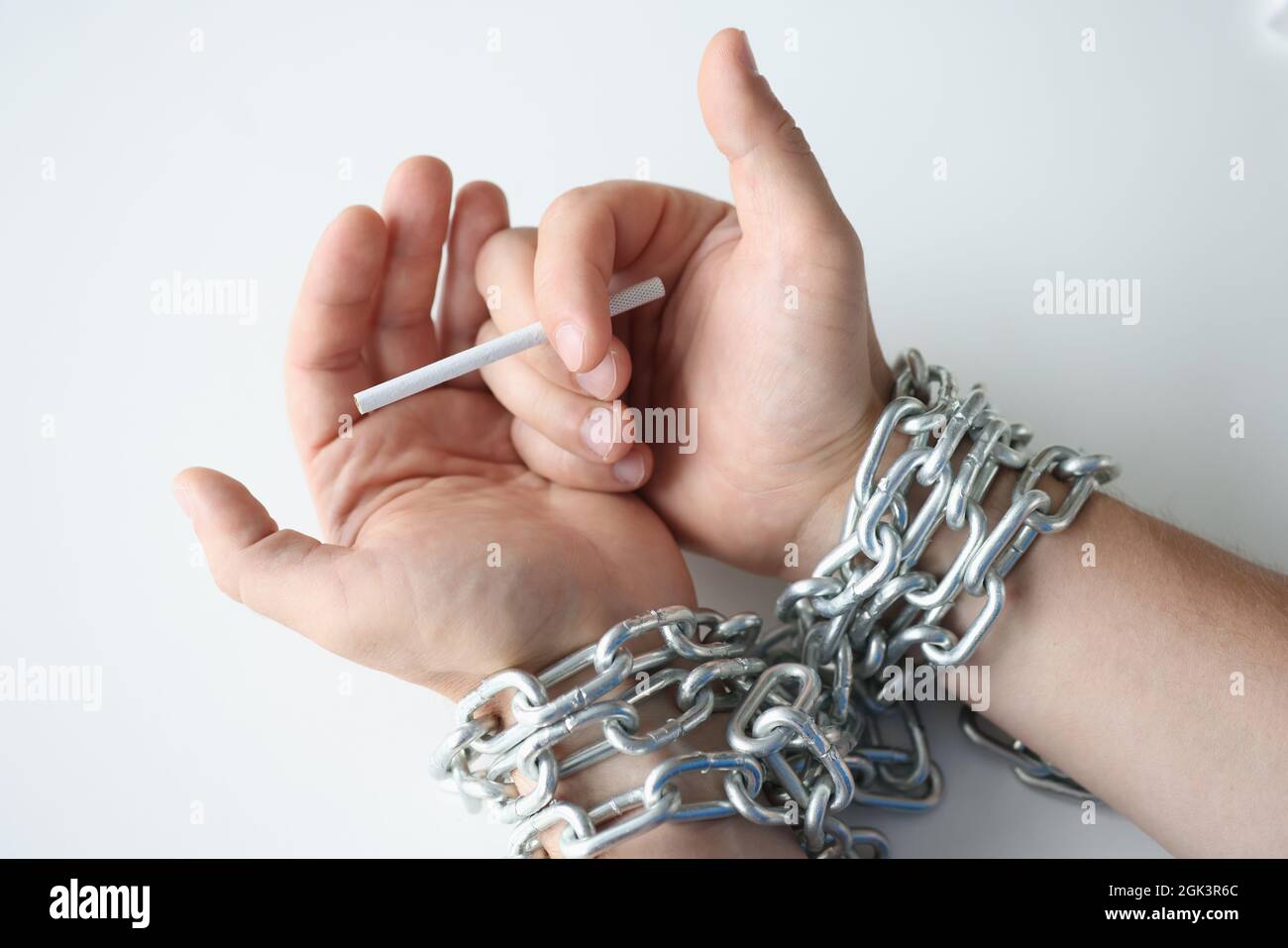 Male hands tied with metal chain holding cigarette on white background ...
