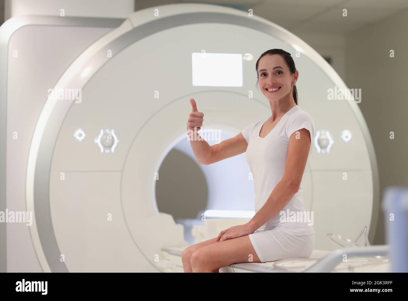 Young woman sitting on magnetic resonance imaging machine and showing ...
