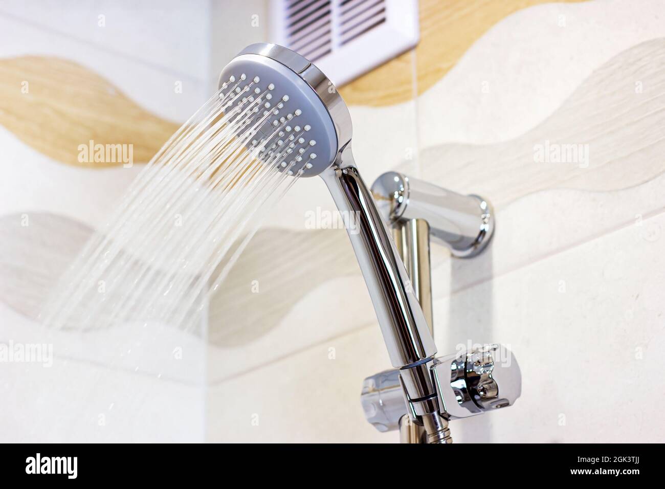 New shiny metal shower head with flowing water on ceramic tile wall ...