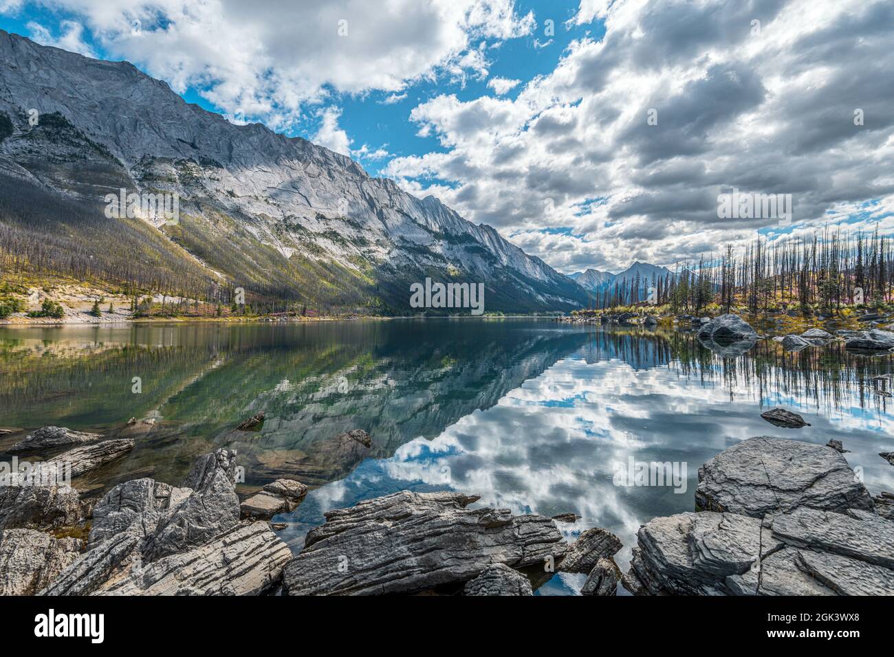 Scene of blue cloudy sky over sunny snowy mountains green reflecting on ...