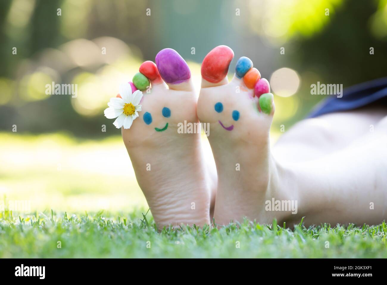 Child feet painted with colorful smiling face in green grass Stock ...