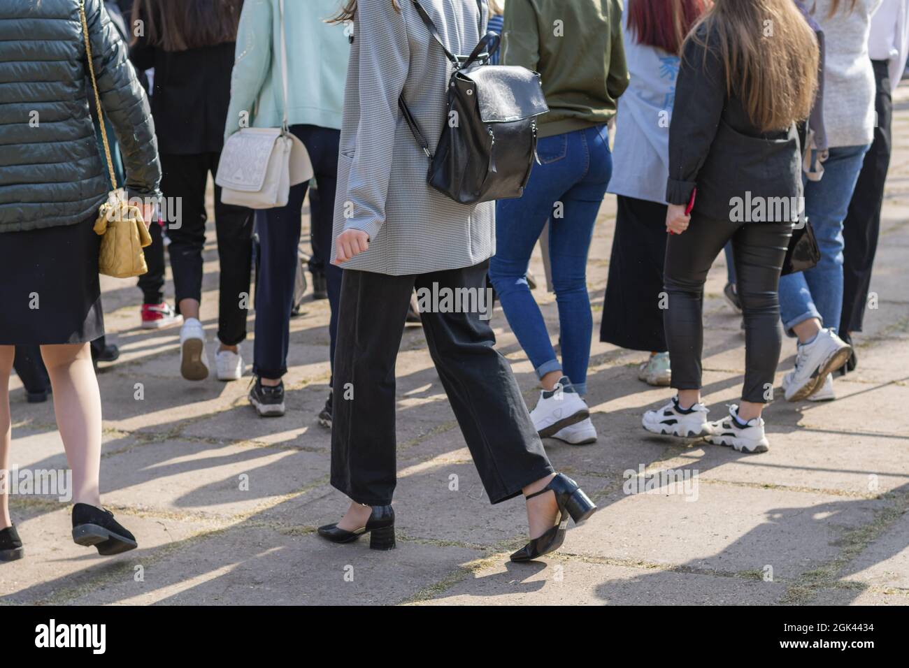 A large group of young people are walking along a city street in ...