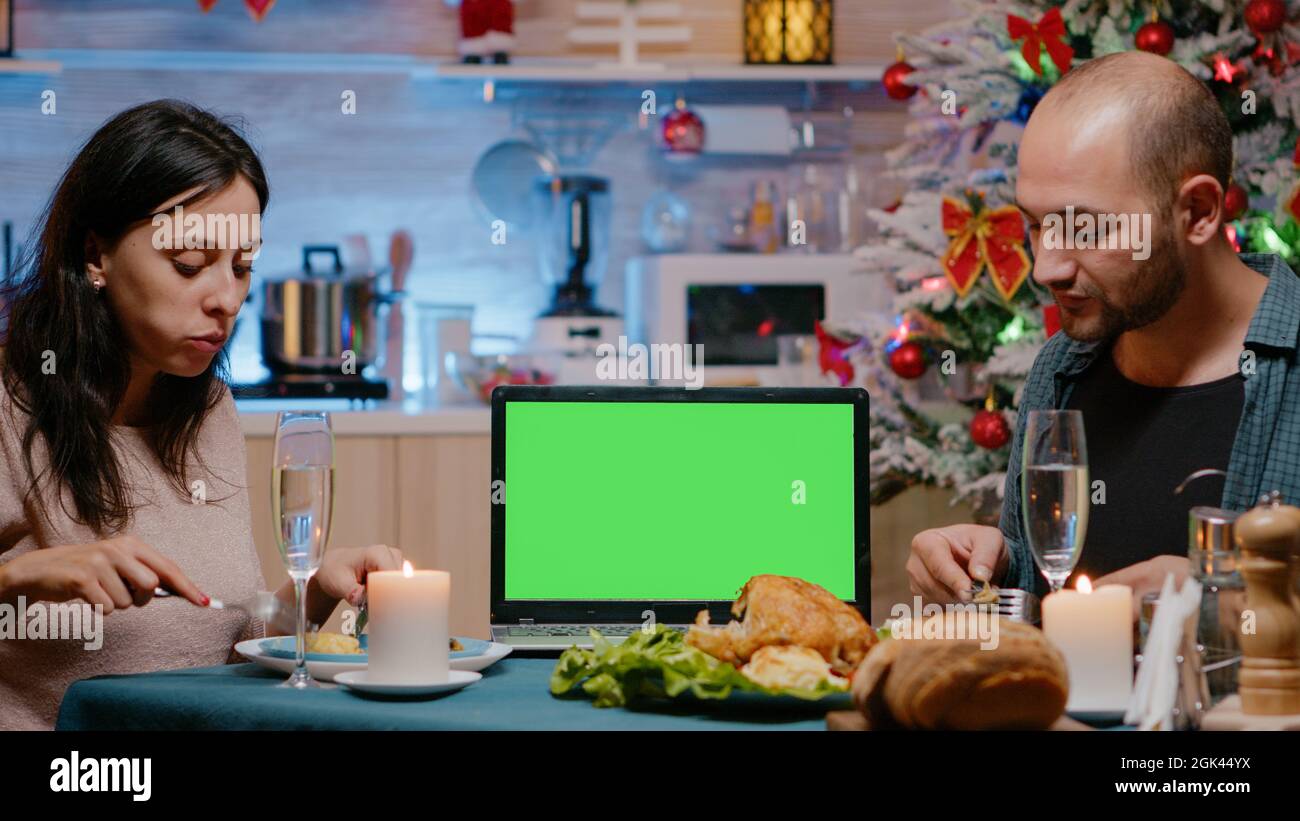 Couple eating festive meal watching horizontal green screen on laptop ...