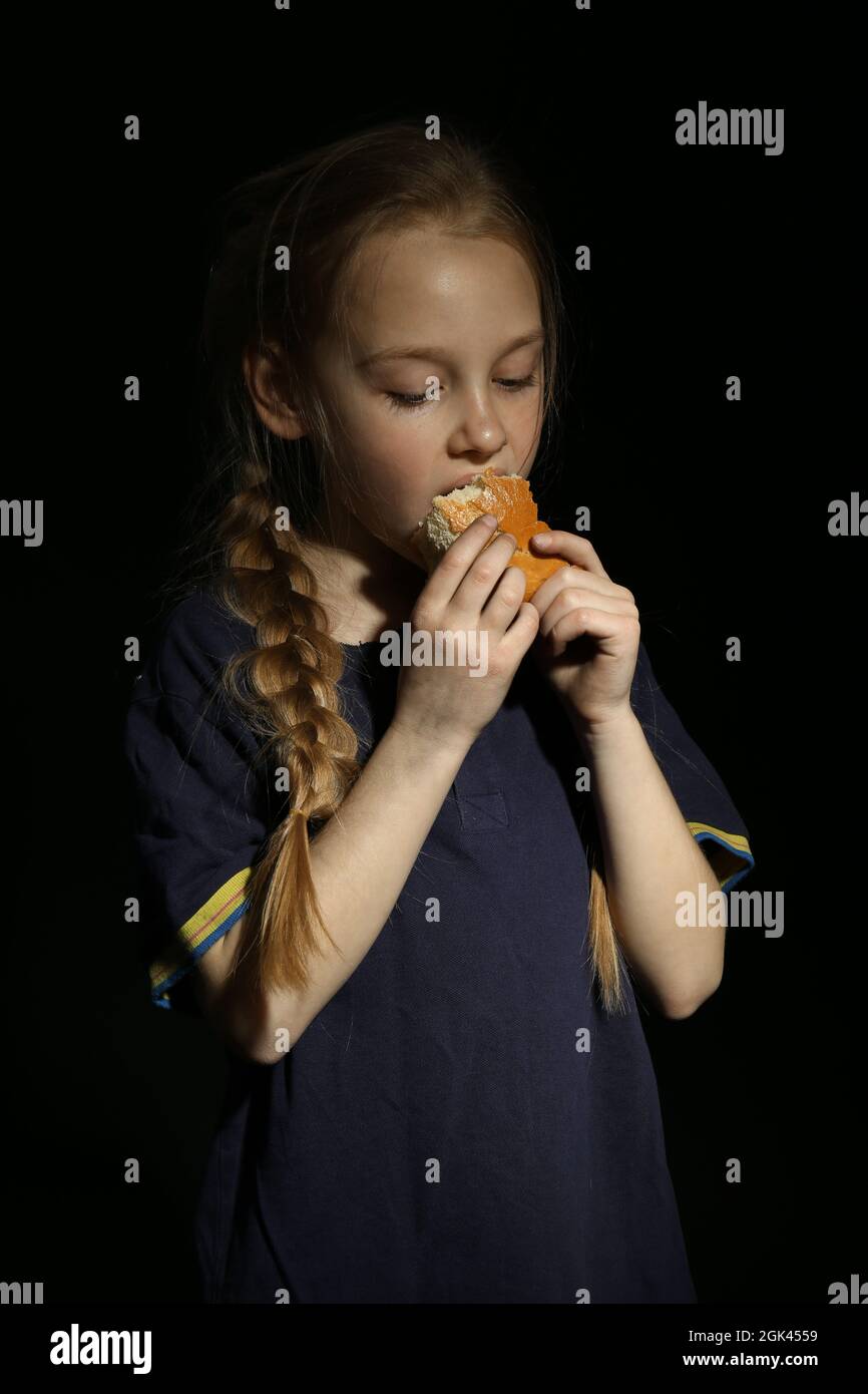 Poor little girl eating bread on black background Stock Photo - Alamy