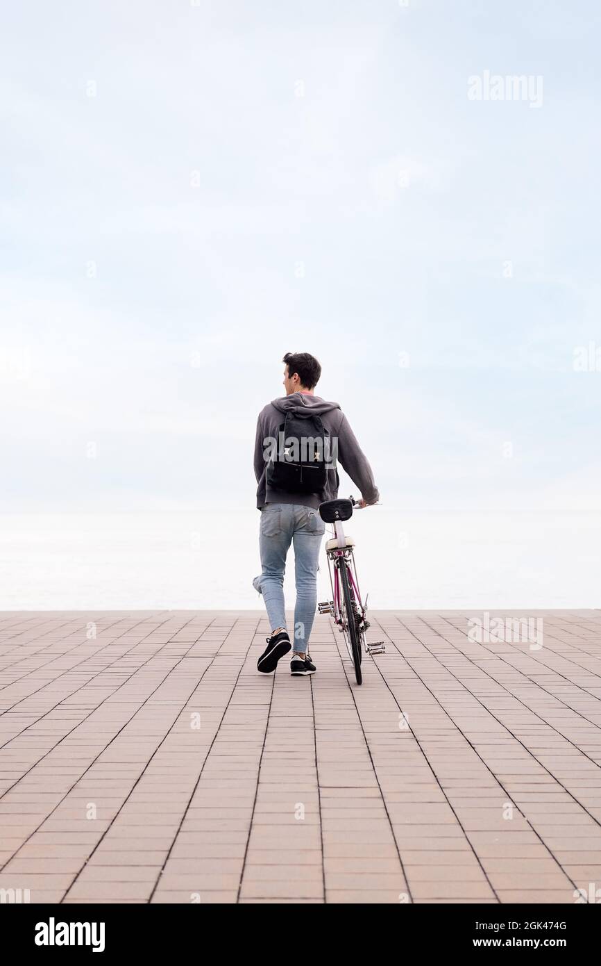 rear view of a young man walking while pushing a bike, concept of ...