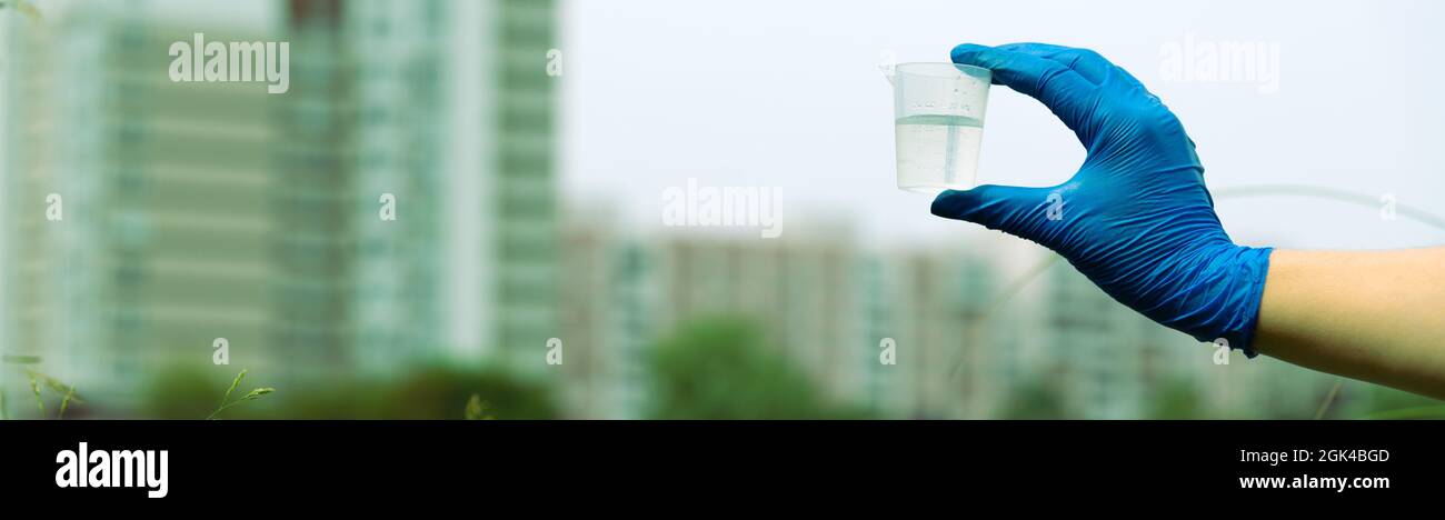A gloved hand holds a beaker with a sample of water. Sampling from open ...