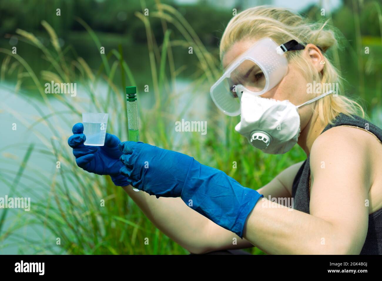 Woman with hands in gloves holds a glass with a sample of water ...
