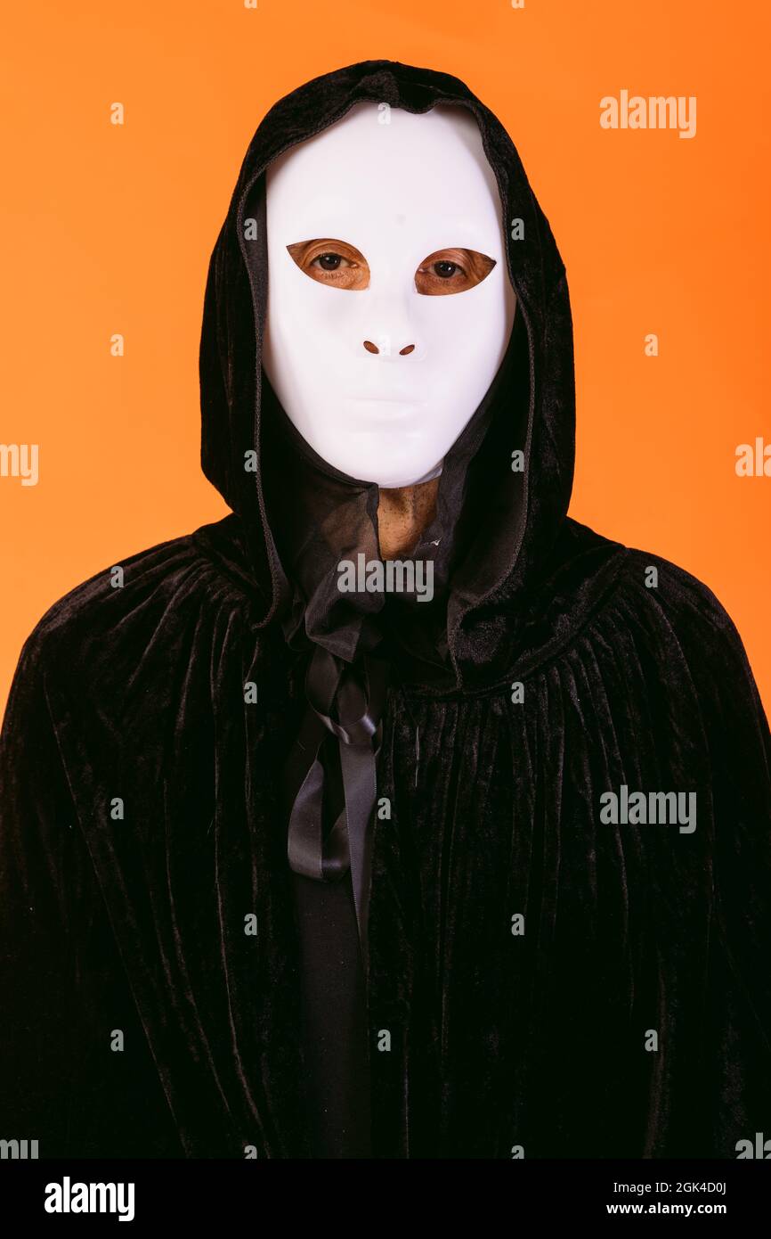 Portrait of a person in white killer Halloween mask, cape and hood ...