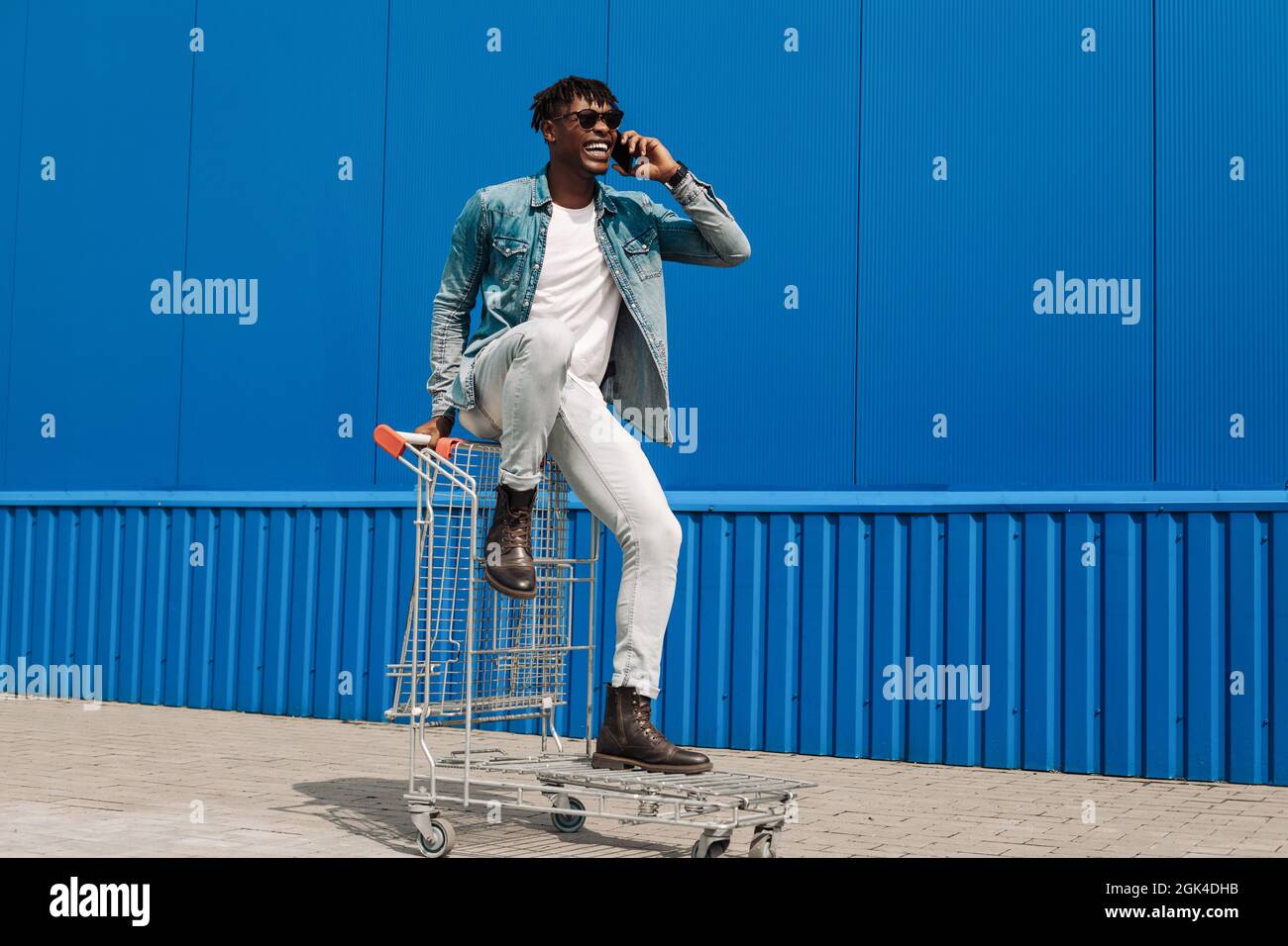 african black man sitting on a shopping cart talking on phone, making a ...