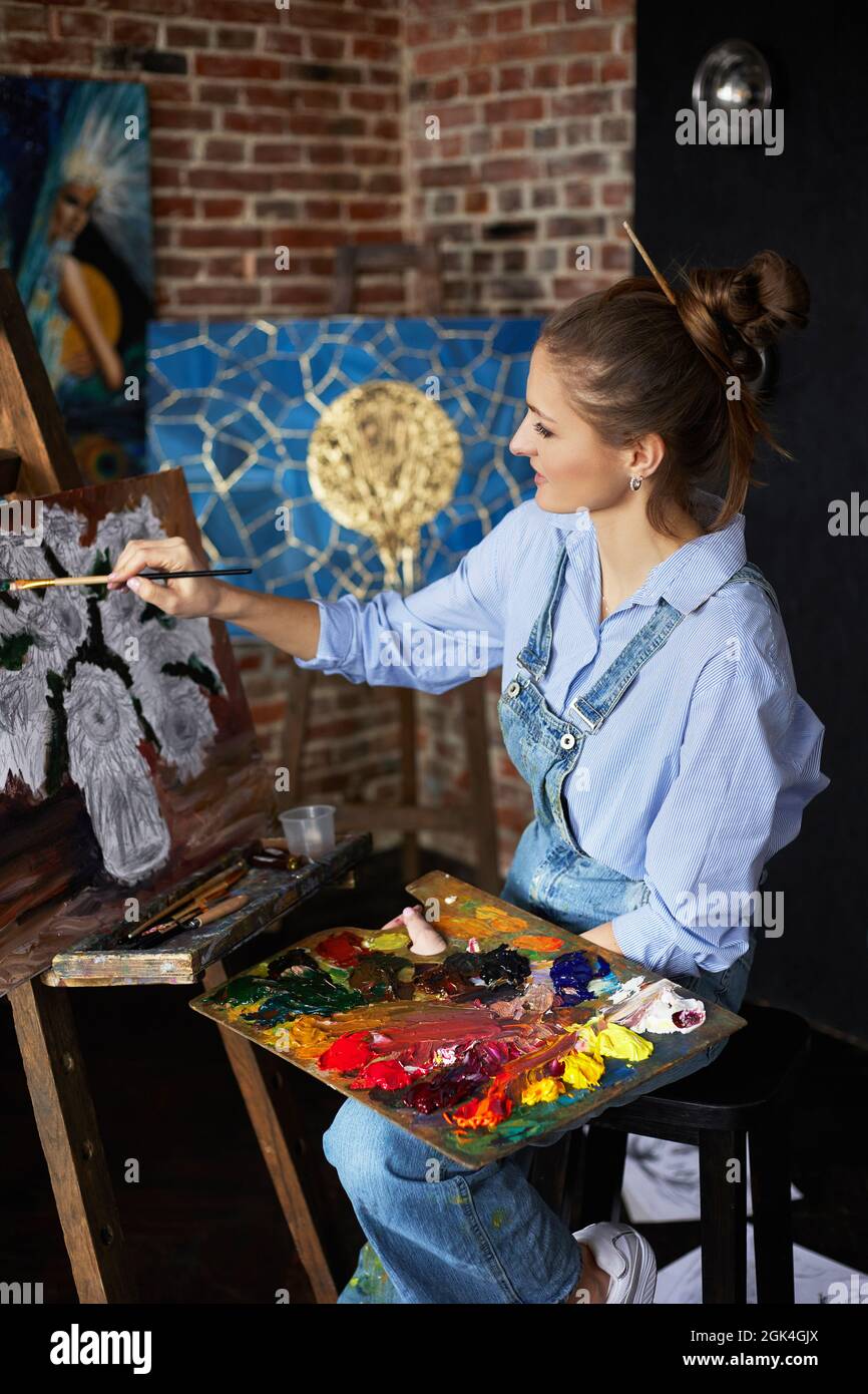 Young beautiful female artist painting still life with sunflower on ...