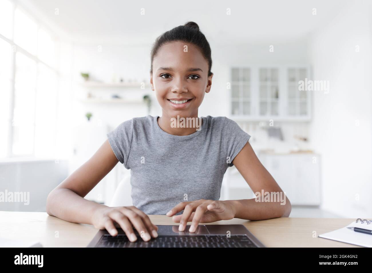 Smiling adolescent afro american girl typing on keyboard and studying ...