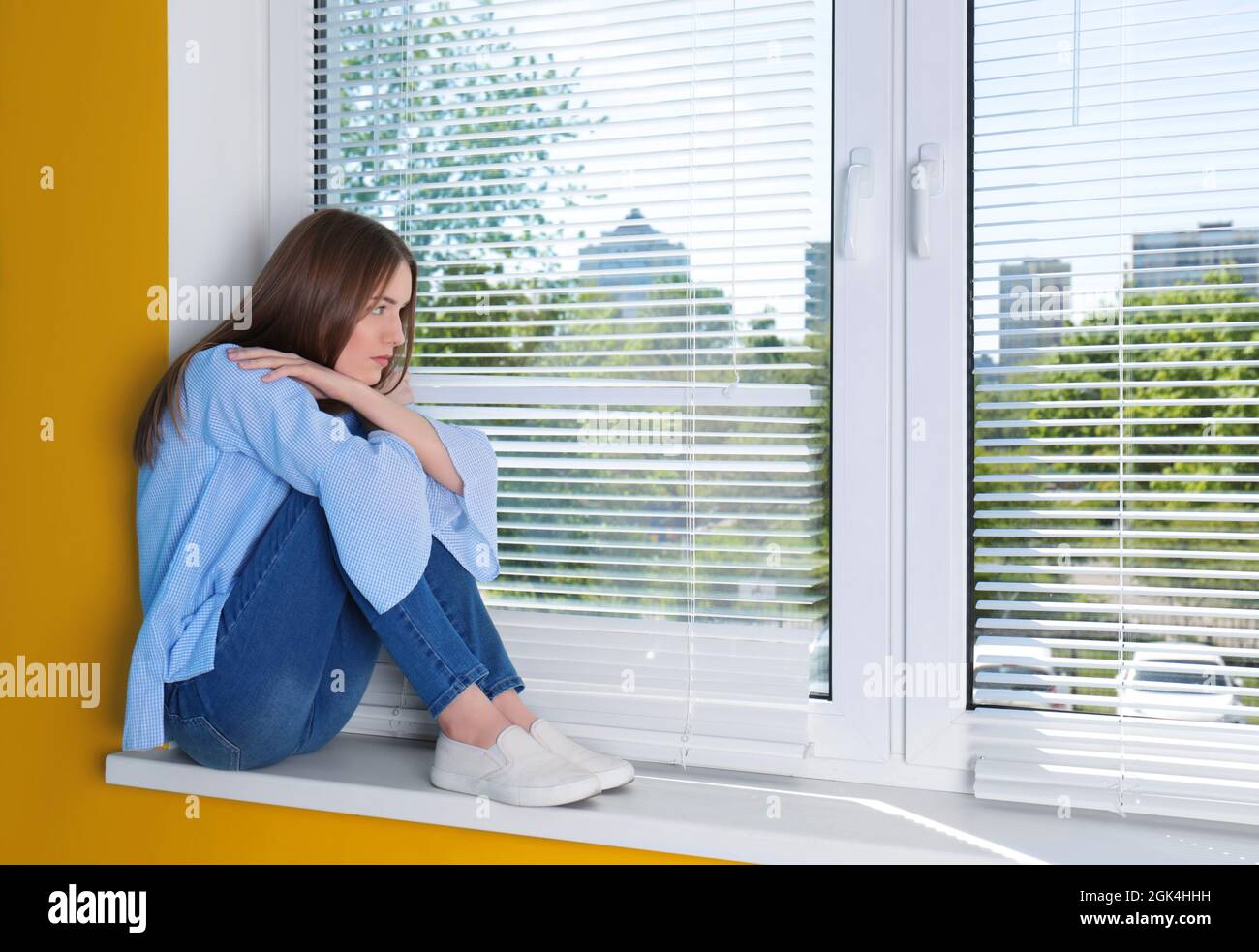 Beautiful sad girl sitting on window sill at home Stock Photo - Alamy