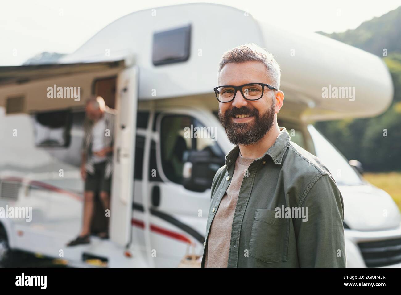 Portrait of happy man standing by car outdoors in campsite, looking at ...