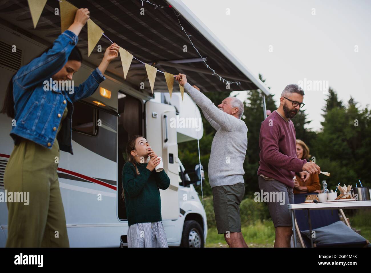 Multi-generation family preparing party by car outdoors in campsite ...