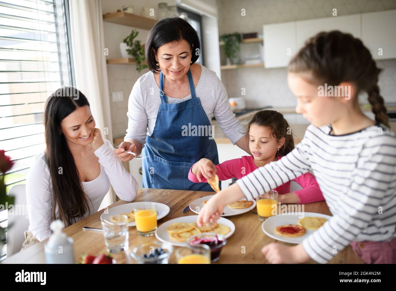 Happy small girls with mother and grandmother eating pancakes indoors ...
