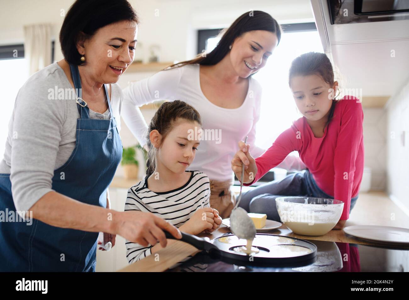 Happy small girls with mother and grandmother making pancakes indoors ...