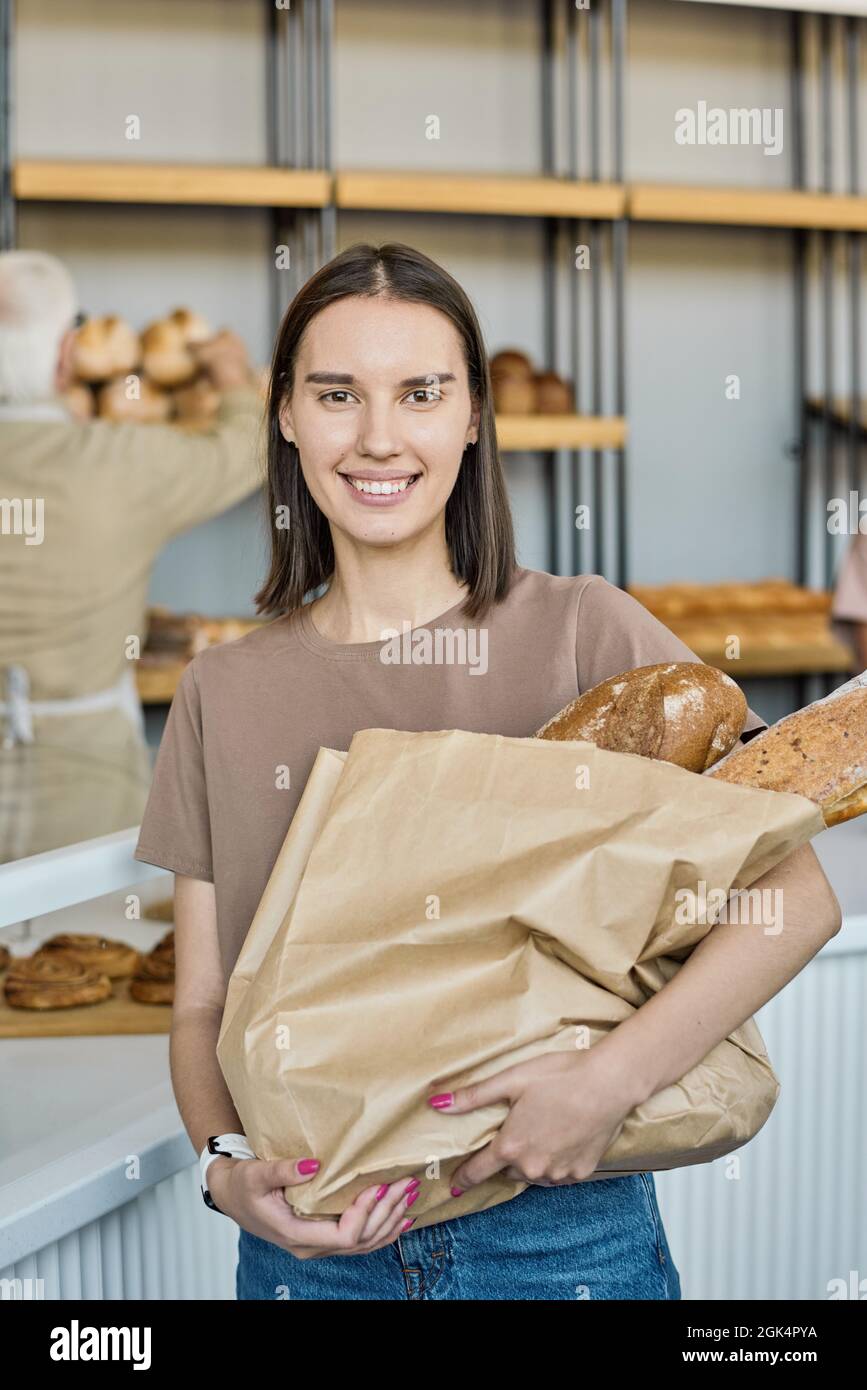 Portrait of happy young female customer standing with paperbag full of ...