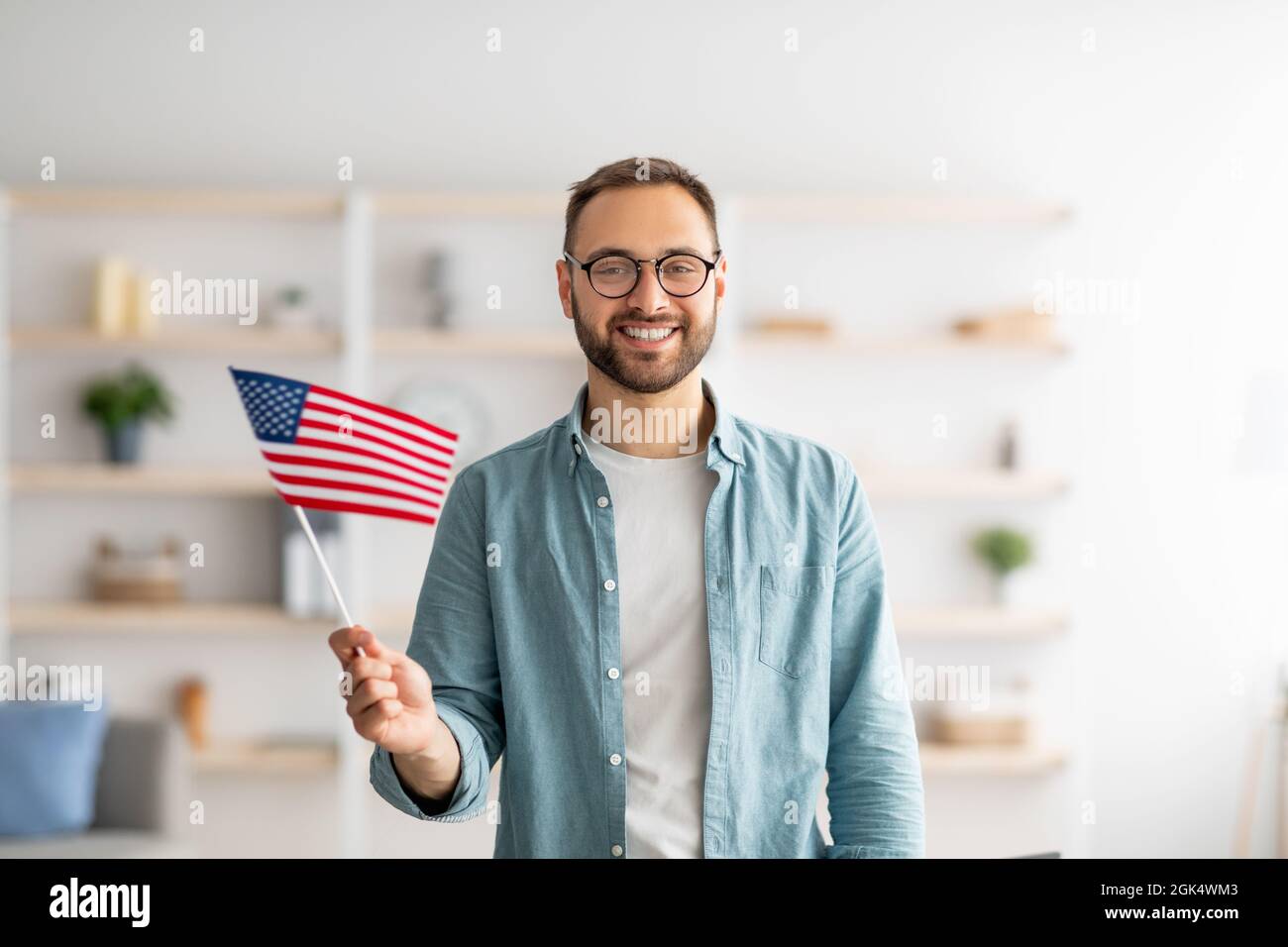 Handsome young guy holding American flag and smiling at camera indoors ...