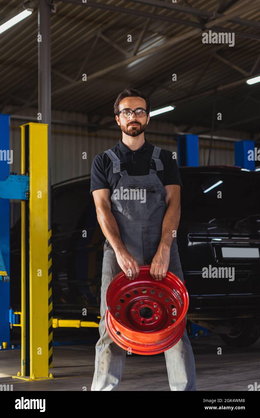 Portrait of young man, male auto mechanic in dungarees working at car service station, indoors ...