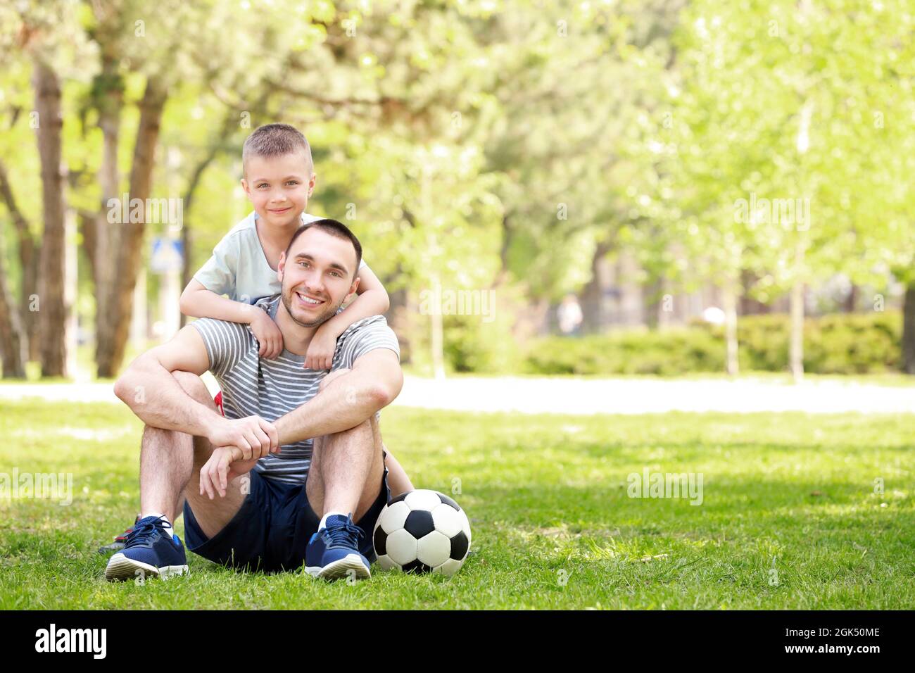 Father and son with soccer ball sitting on green grass in park Stock ...