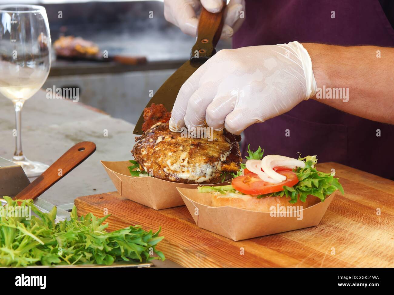 A chef prepares a burger for a customer. A man wearing white protective ...