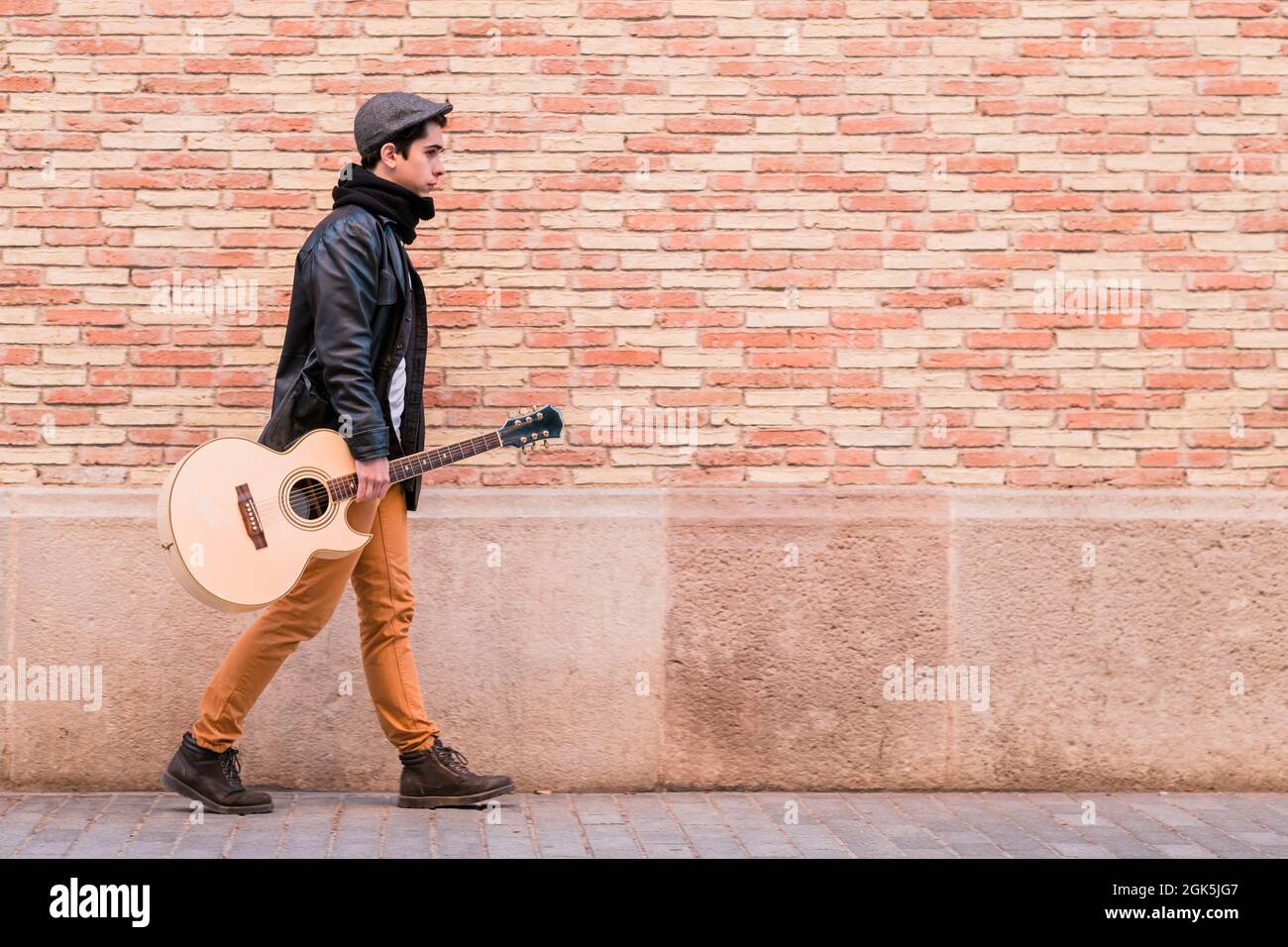 Street musician walking with acoustic guitar. Young handsom man wearing ...