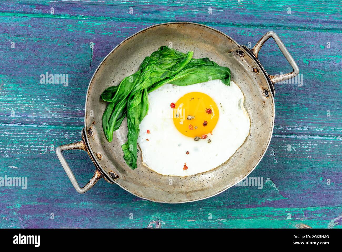 Rustic pan with fried egg and steam cooked spinach on a green-purple ...