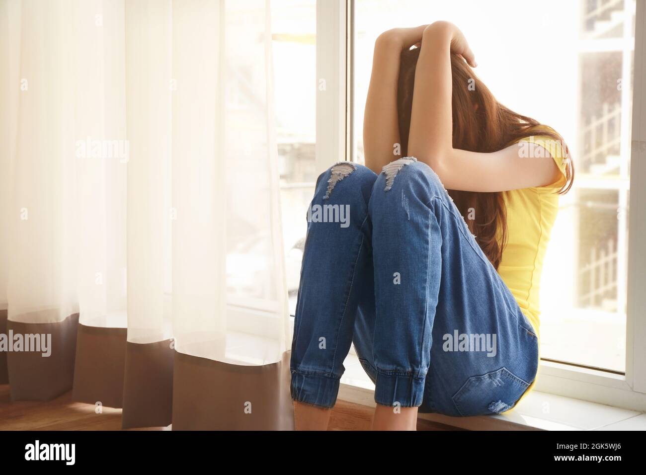 Sad pretty girl sitting on window sill at home Stock Photo - Alamy
