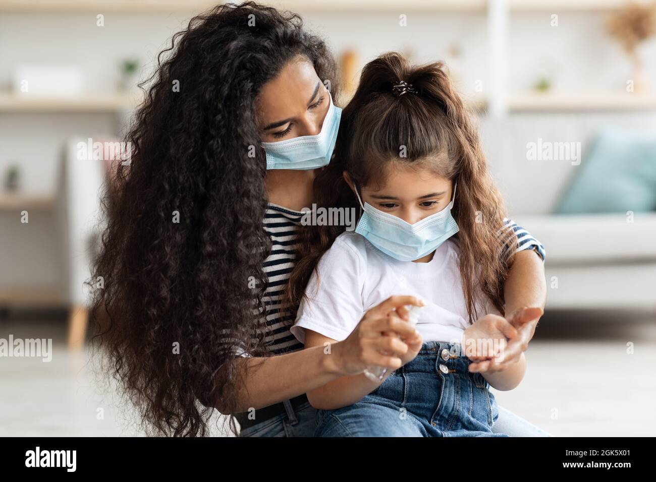 Middle-eastern mother and daughter in face masks using disinfectant ...